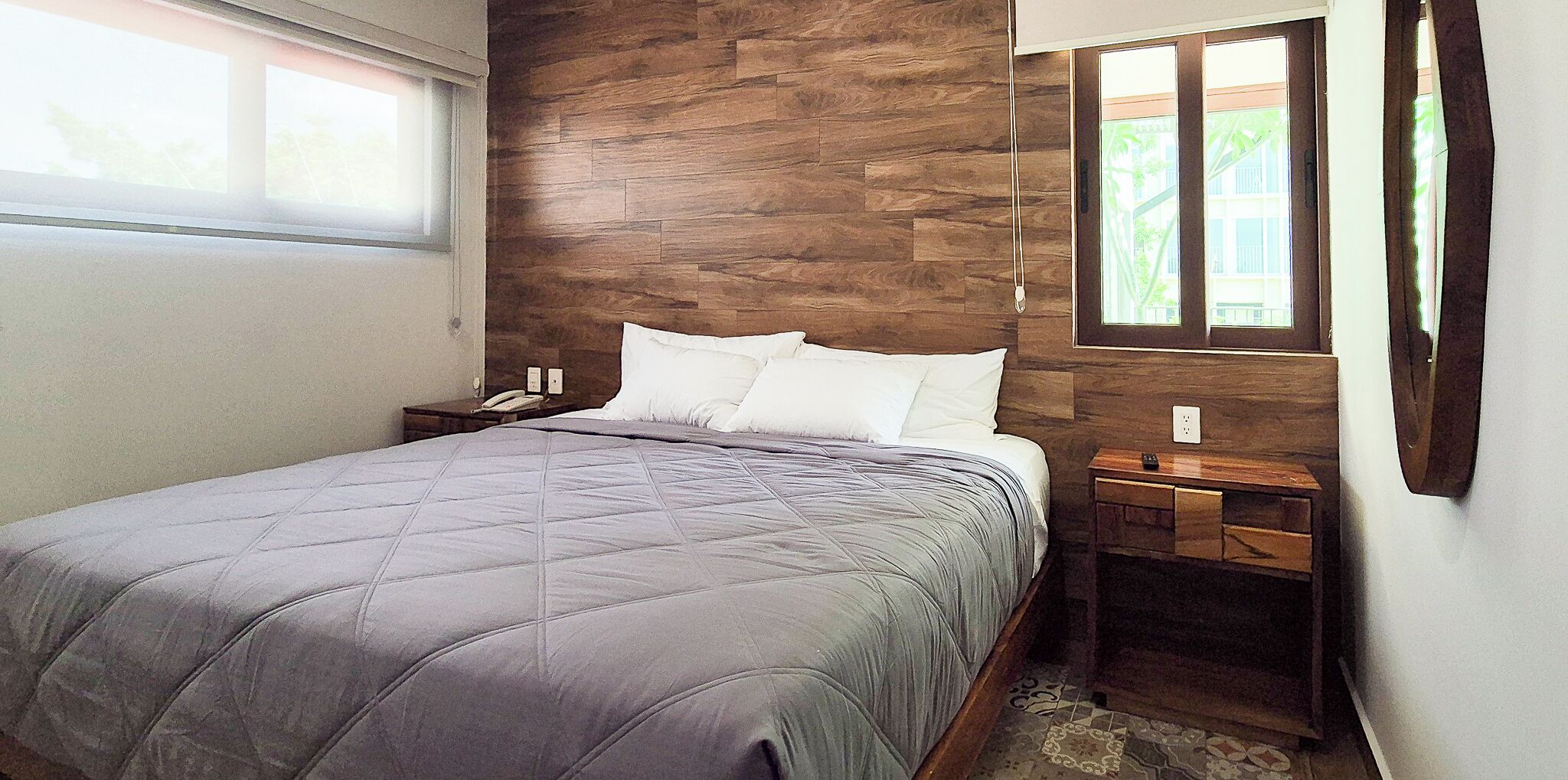 Quarto com cama, mesas de cabeceira, painel de madeira, janela e espelho.