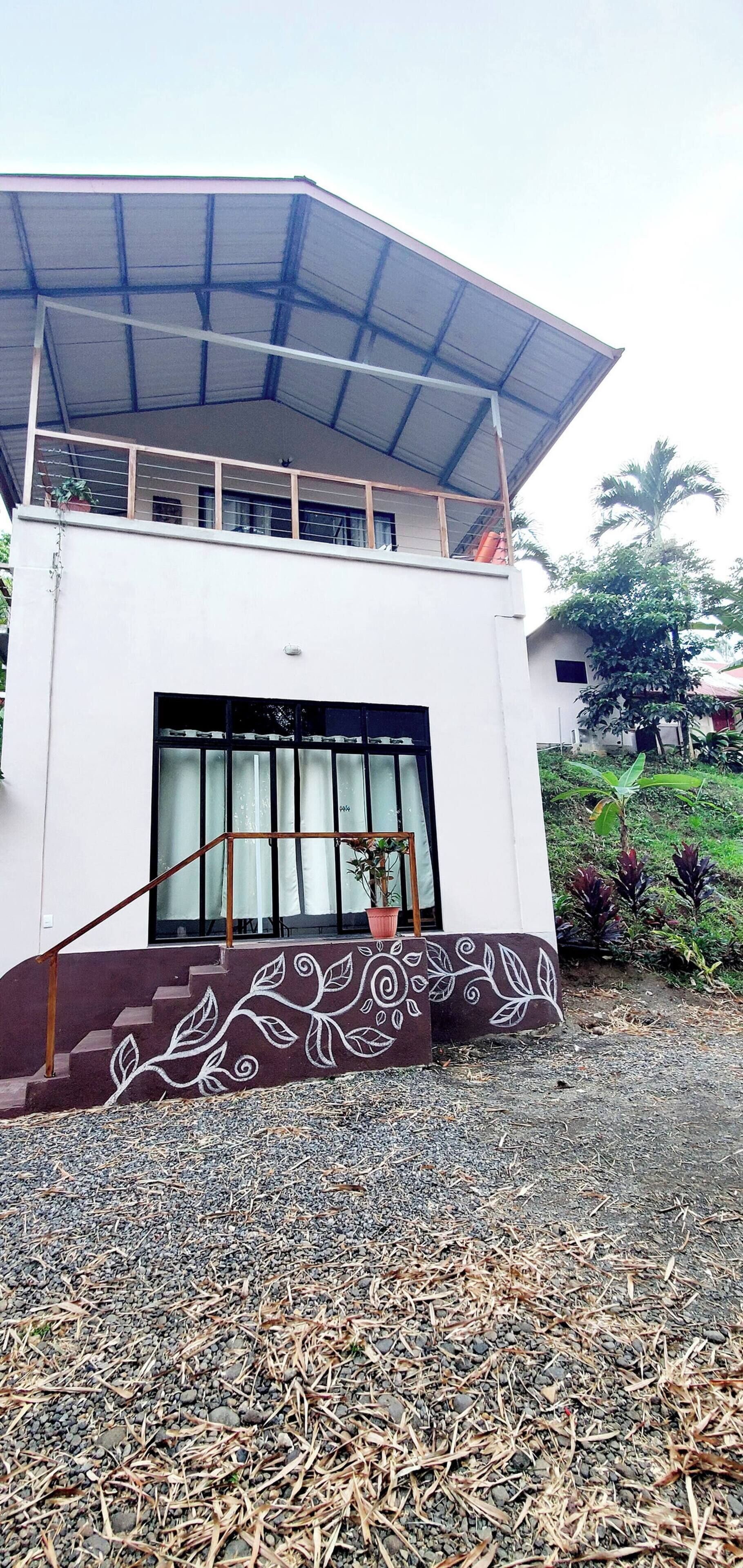 Um edifício moderno com telhado plano, uma janela grande e uma escadaria que leva a uma varanda.
