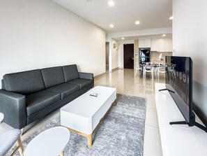 Uma sala de estar moderna com um sofá cinzento, uma mesa de centro branca e uma televisão de tela plana.