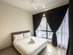Quarto de hotel com cama, ventilador de teto, janela com cortinas e vista para a cidade.
