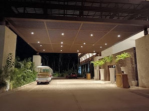 Uma entrada coberta com um veículo, um edifício com telhado inclinado e plantas em vasos.