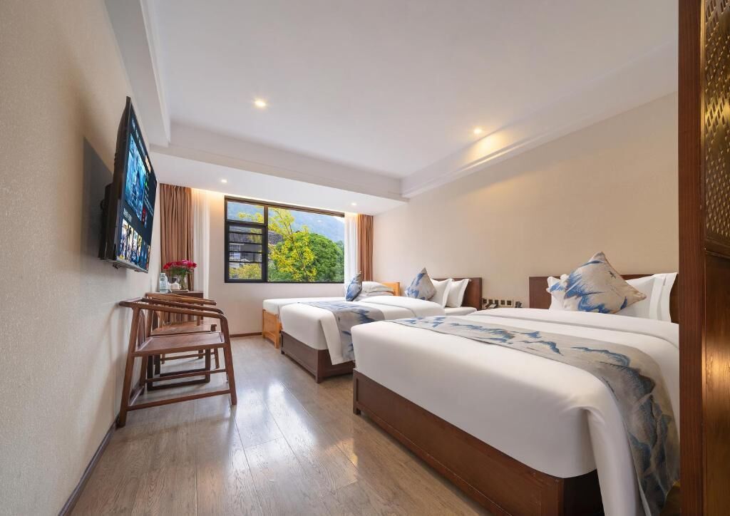 Quarto de hotel com duas camas, televisão, escrivaninha e janela com vista para o verde.