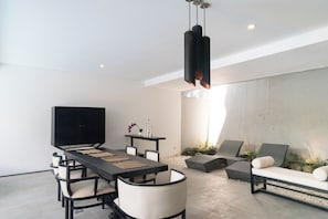 Uma sala de estar moderna com área de jantar, televisão de tela plana e um espaço de estar com almofadas e parede de pedra.