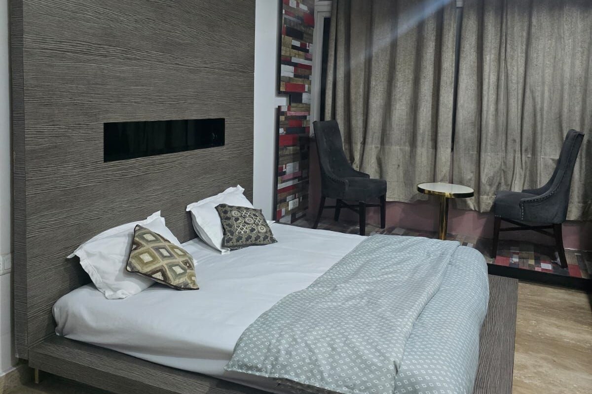 Quarto moderno com cama, duas cadeiras, uma mesinha e ventoinha no teto.