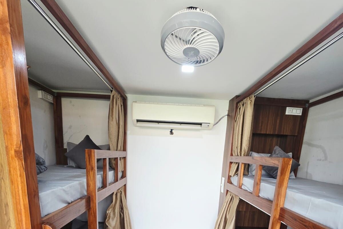 Um corredor estreito com beliches em ambos os lados, um ventilador de teto e um aparelho de ar condicionado.