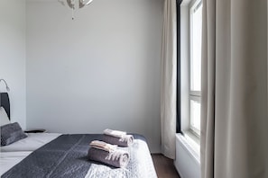 Quarto com cama, radiador e janela com cortinas.