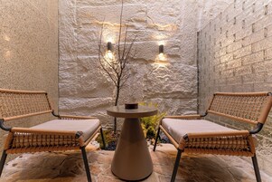 Mural de pedra com duas cadeiras de vime e uma mesa, cada uma com uma vela.