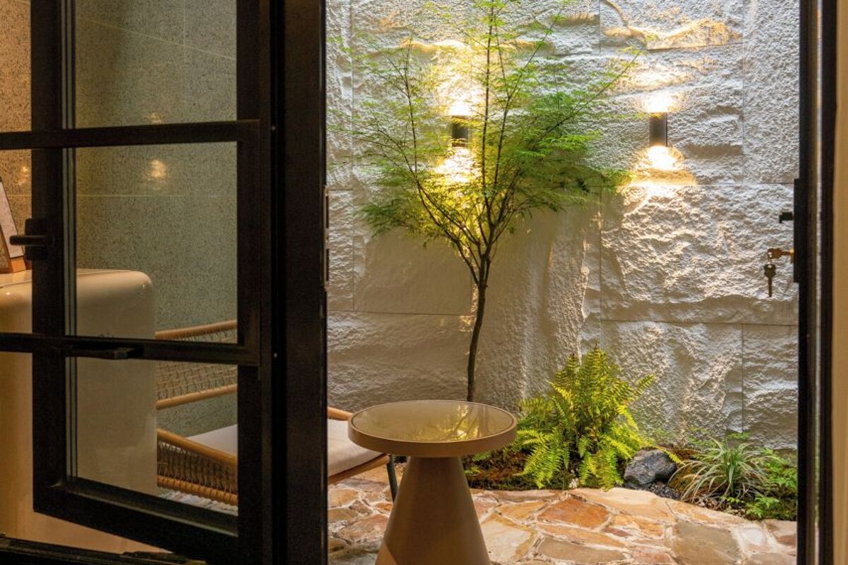 Um pátio de pedra com mesa e cadeiras, uma árvore e um muro com trabalho em pedra texturizada.
