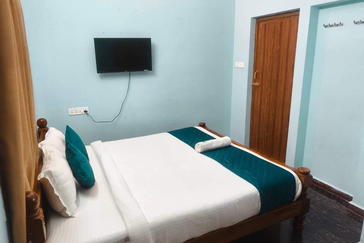 Uma cama de solteiro com estrutura de madeira, uma televisão de tela plana presa à parede e uma porta com painel de madeira.
