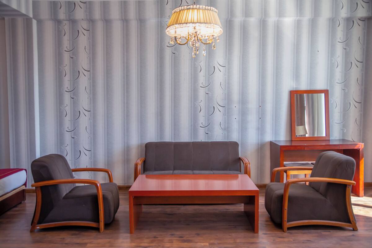 Quarto com sofá, duas poltronas, mesa de centro de madeira, candelabro, espelho e cama.