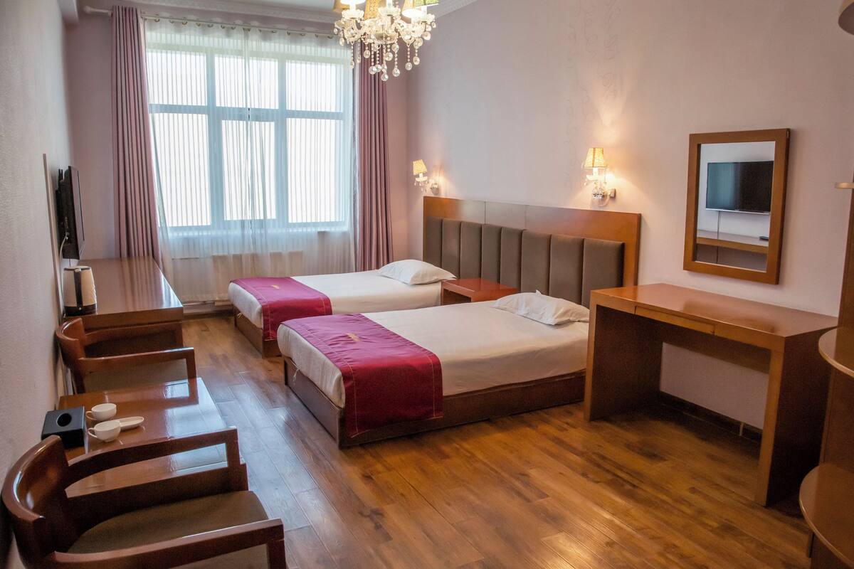 Quarto de hotel com duas camas, uma escrivaninha, televisão e um candelabro.