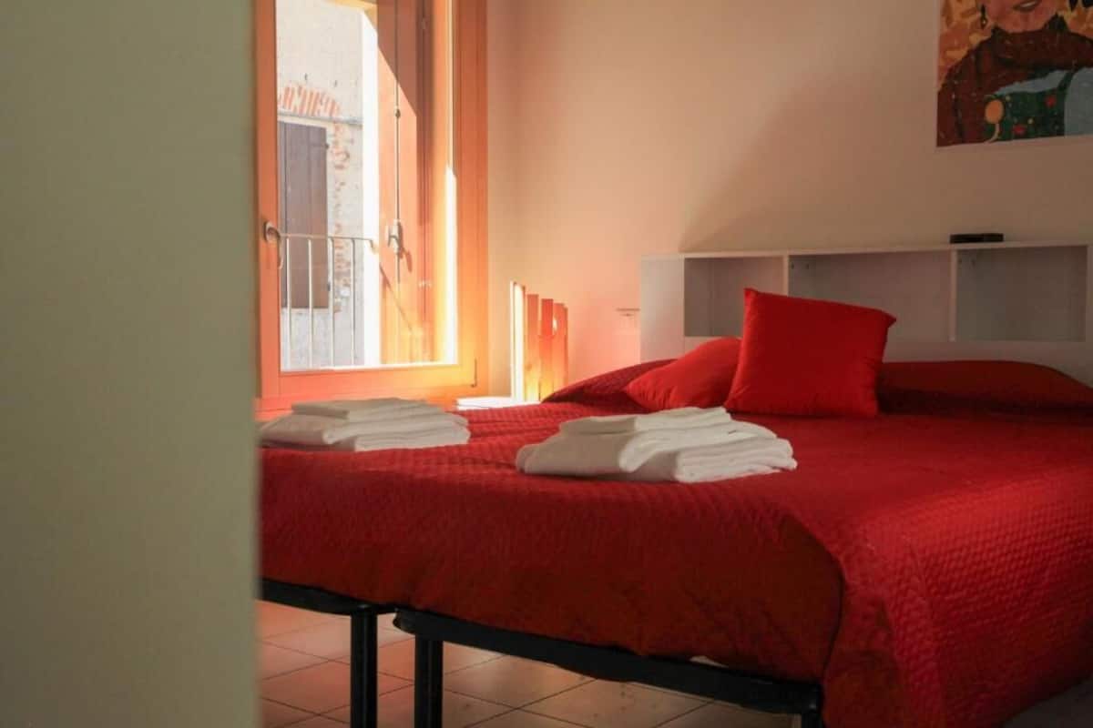 Quarto com cama, toalhas brancas, janela com vista e um quadro na parede.