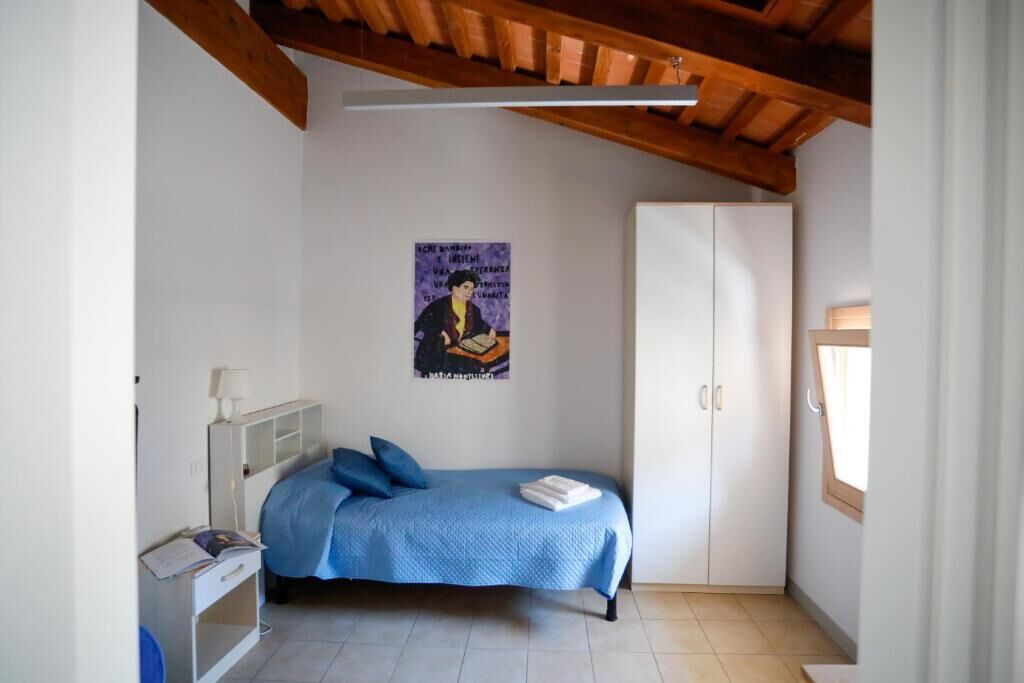 Quarto com cama, guarda-roupa, escrivaninha com abajur e um quadro na parede.