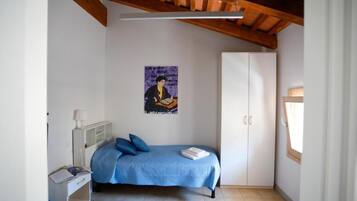 Quarto com cama, guarda-roupa, escrivaninha com abajur e um quadro na parede.
