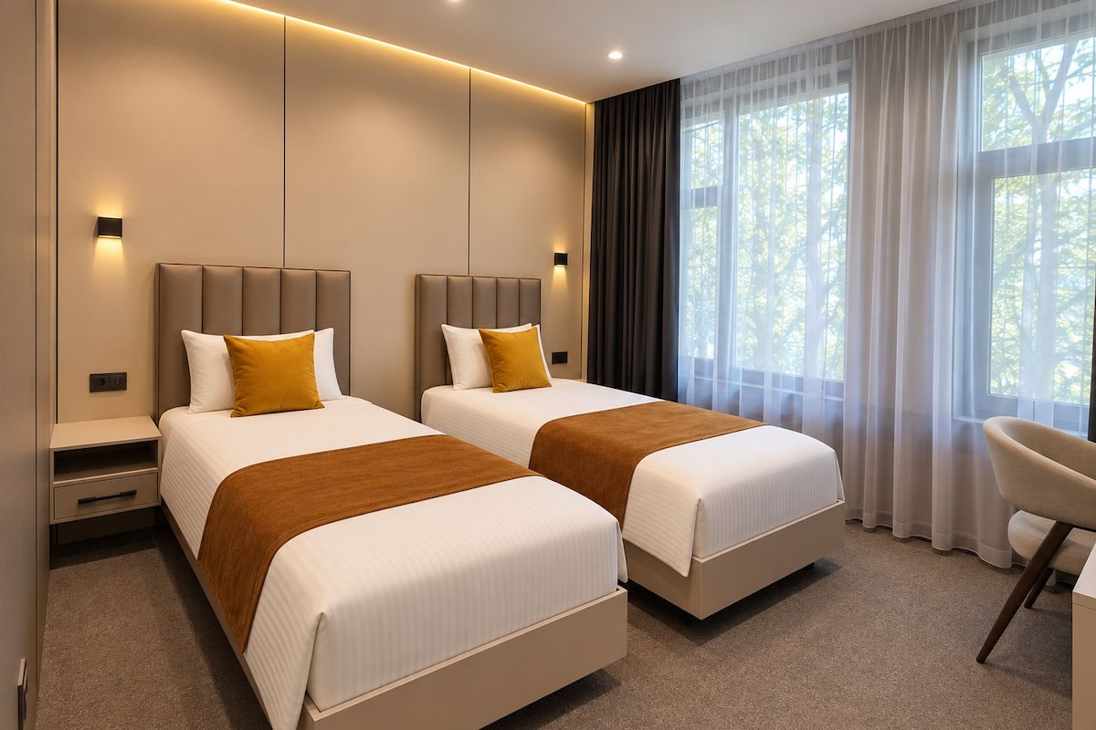 Quarto de hotel com duas camas, uma cadeira e uma janela grande com cortinas.