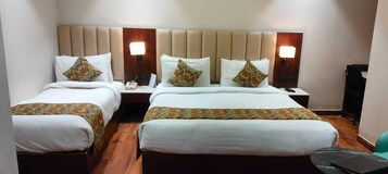 Quarto de hotel com duas camas, uma mesa de cabeceira com abajur, uma escrivaninha e uma cadeira.