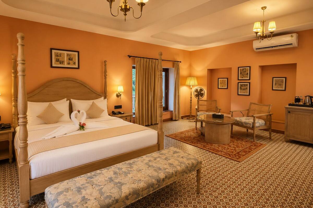 Quarto de hotel com cama de dossel, um banco, uma escrivaninha com cadeira, um ventilador e uma cafeteira.