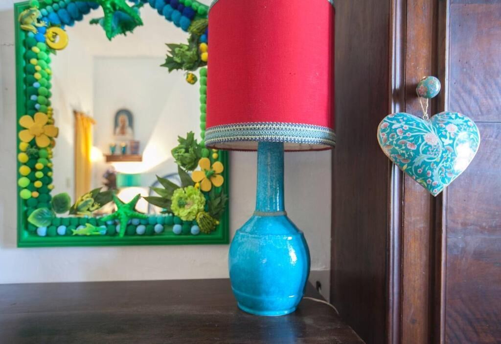 Um abajur azul com cúpula vermelha, um objeto decorativo em formato de coração e um espelho com moldura verde.