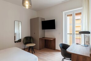 Quarto de hotel moderno com cama, escrivaninha, cadeira, televisão e janela com vista para edifícios.