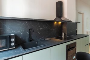 Cozinha moderna com bancada de mármore preto, micro-ondas embutido, pia e fogão.