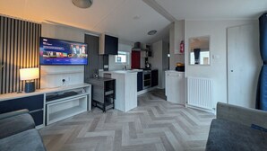 Uma sala de estar moderna com televisão de tela plana, um sofá, cozinha com micro-ondas e área de refeições.