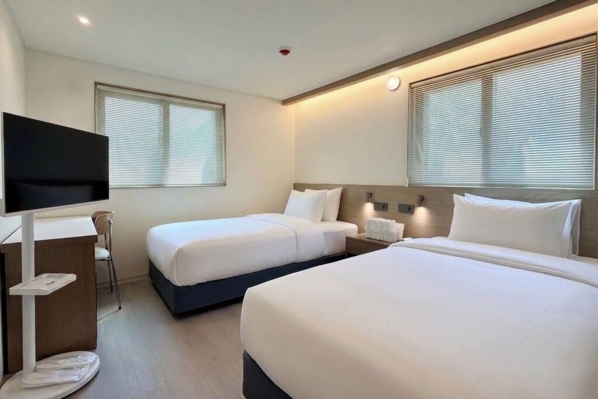Quarto de hotel com duas camas, uma escrivaninha, uma televisão e um pequeno espaço de estar.