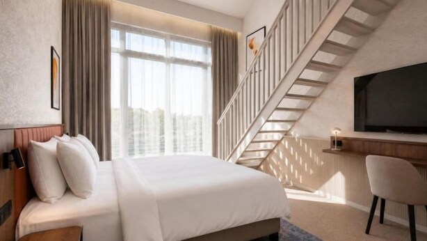 Quarto de hotel com cama, escrivaninha, cadeira, televisão e escada.