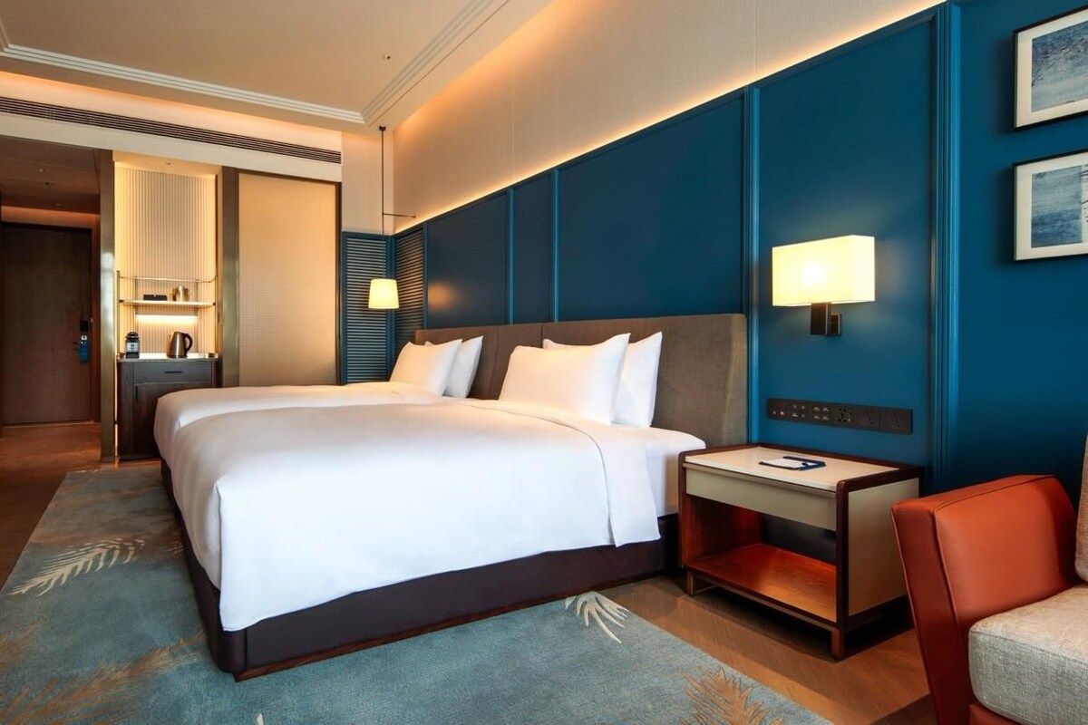 Quarto de hotel com uma cama grande, mesas de cabeceira, escrivaninha e uma cadeira.