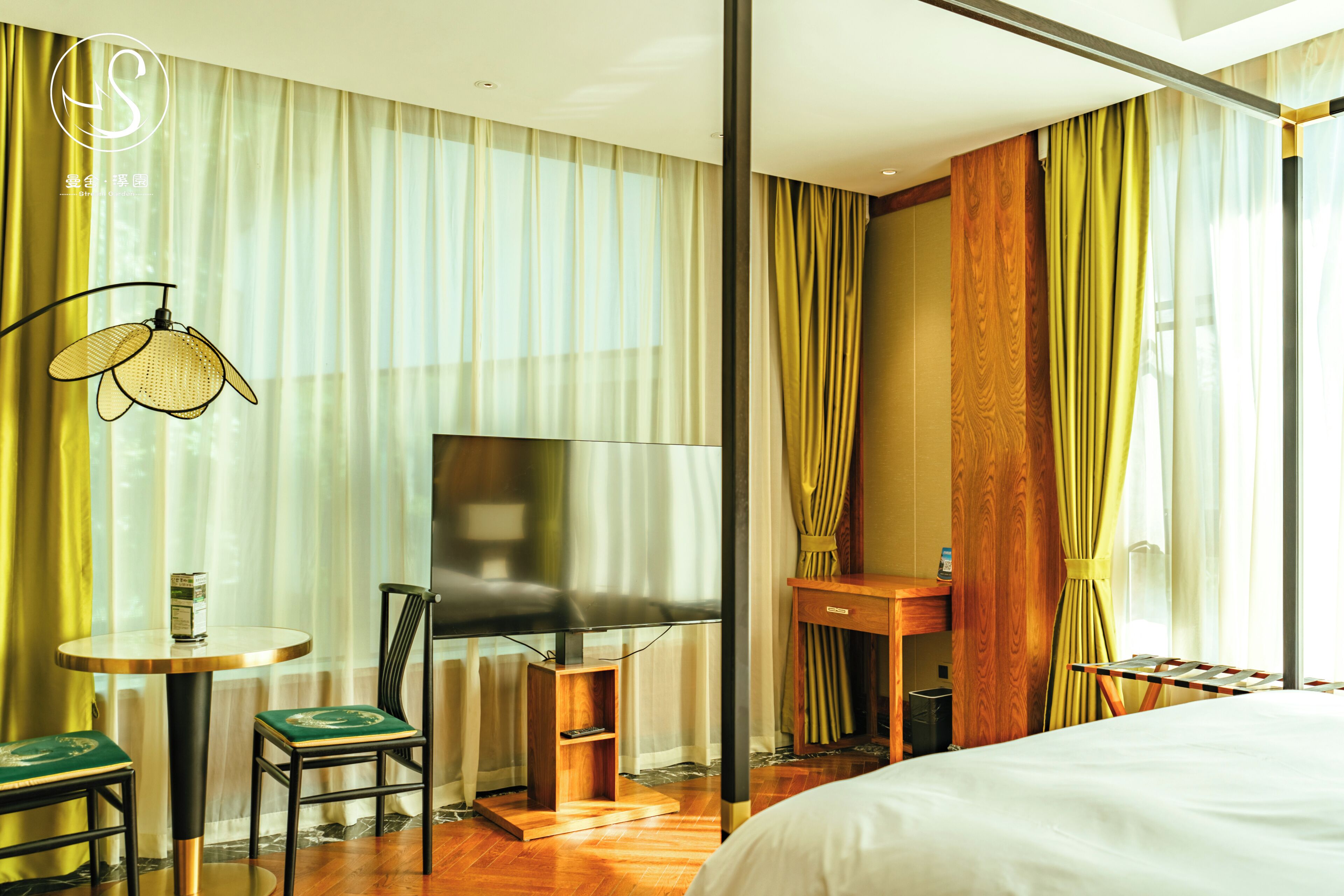 Quarto de hotel com cama, televisão, mesinha com cadeiras e escrivaninha com cadeira.