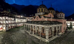 Um edifício histórico com várias cúpulas e arcos, rodeado por um pátio com pavimento de pedra.