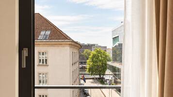 Janela com vista para um edifício com telhado de azulejos e uma árvore ao primeiro plano.