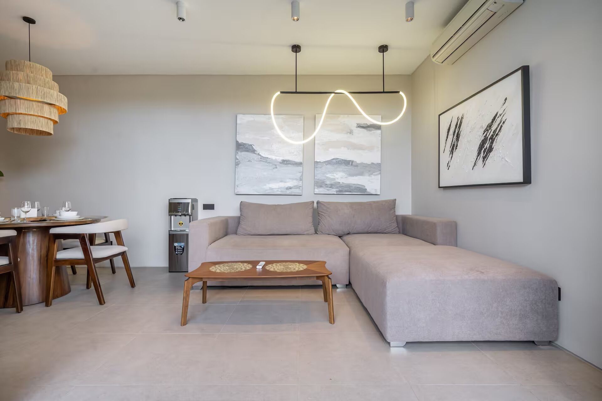 Uma sala de estar moderna com um sofá seccional, uma mesa de jantar redonda, uma máquina de café e arte abstrata na parede.