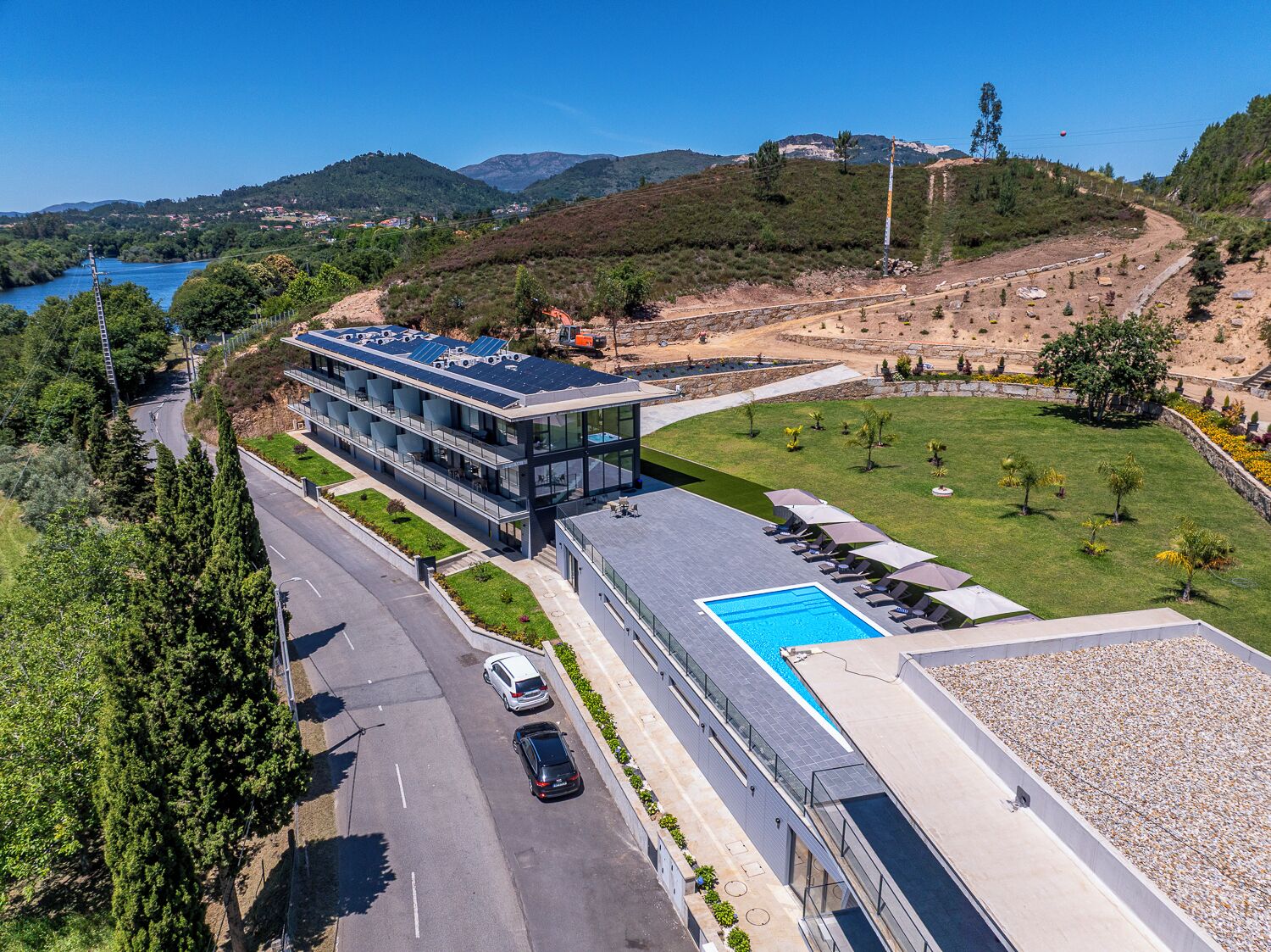 Um hotel moderno com piscina, área de estacionamento e vista para a paisagem circundante.
