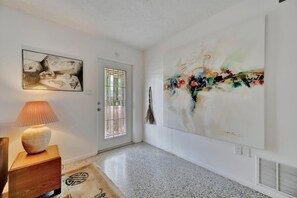 Um corredor com uma porta, uma luminária, um tapete e duas obras de arte nas paredes.