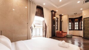 Um quarto espaçoso com uma cama grande, um espaço de estar com sofá e banquinho, e vista para o exterior.