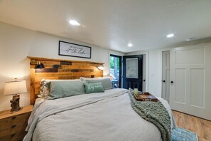 Quarto com cabeceira de madeira, cama com travesseiro verde, abajur e uma frase emoldurada na parede.