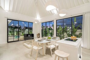 Uma sala de jantar espaçosa com uma mesa grande, cadeiras e vista para uma piscina e vegetação lá fora.