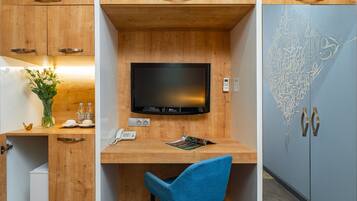 Quarto compacto com uma escrivaninha de madeira, uma cadeira azul, uma televisão e um frigorífico com decoração em relevo.