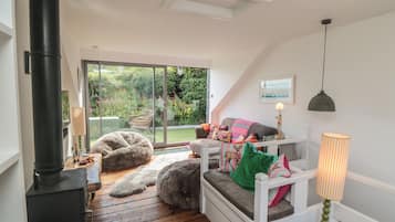Quarto acolhedor com lareira, um sofá com almofadas, uma luminária e vista para um jardim através de uma porta deslizante.