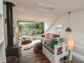 Quarto acolhedor com lareira, um sofá com almofadas, uma luminária e vista para um jardim através de uma porta deslizante.