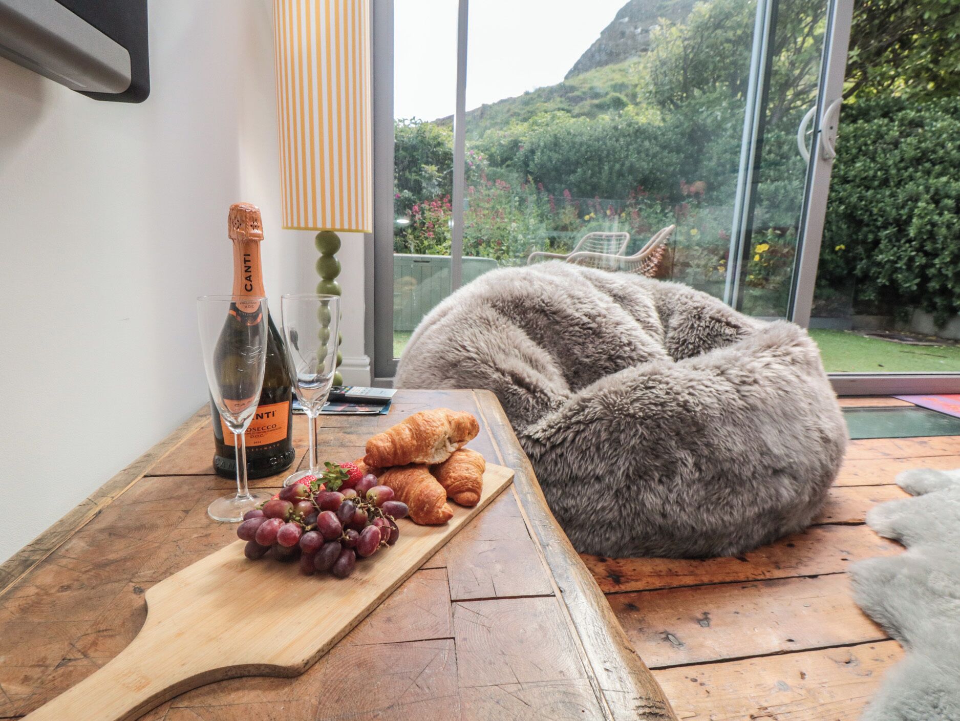 Uma área de estar ao ar livre acolhedora, com mesa de madeira, garrafa de vinho, taça, uvas e croissants.