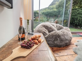 Uma área de estar ao ar livre acolhedora, com mesa de madeira, garrafa de vinho, taça, uvas e croissants.