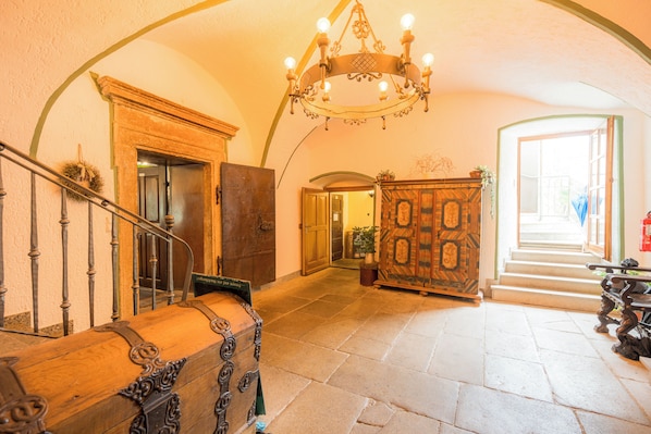 Um espaço amplo com escada, um banco de madeira, um candelabro e uma porta que dá para outro quarto.