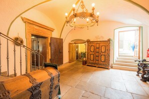 Um espaço amplo com escada, um banco de madeira, um candelabro e uma porta que dá para outro quarto.