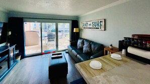 Uma sala de estar com um sofá, uma mesa de centro e uma placa com a inscrição 'SAND AND SURF'.