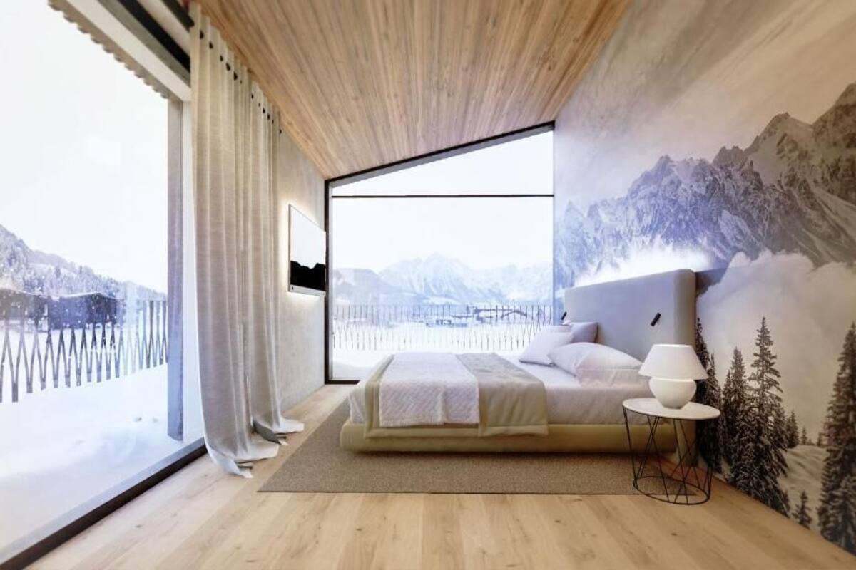 Quarto com uma grande janela, cama, mesa de cabeceira e um mural de montanhas.