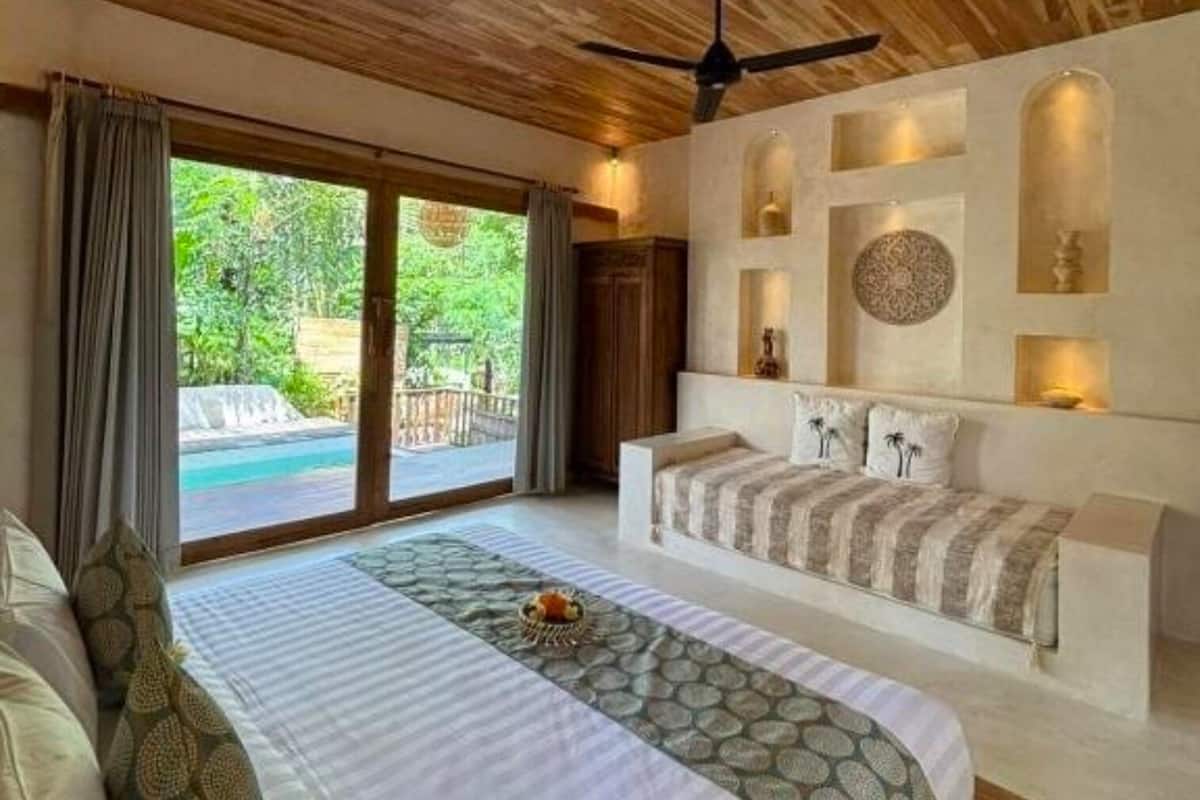 Quarto com uma cama grande, um sofá, um ventilador de teto e vista para uma piscina.