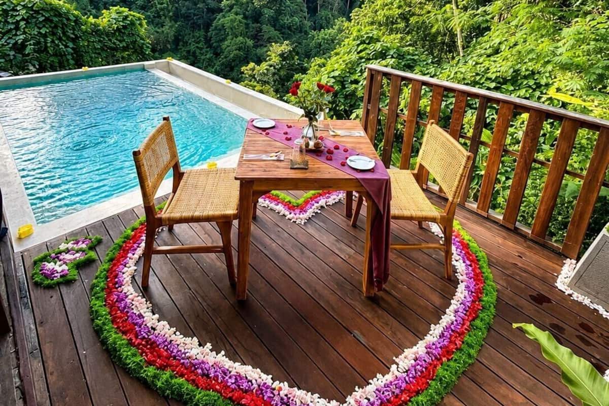 Um deck de madeira com piscina, cercado por vegetação exuberante e um tapete em formato de coração.