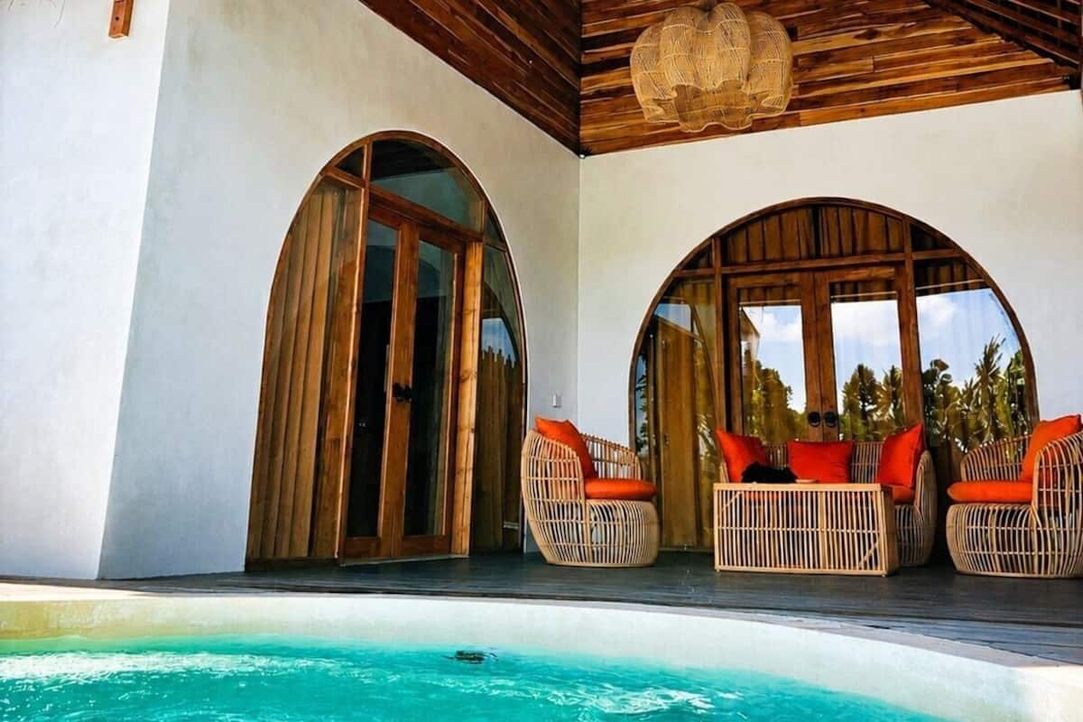 Área de piscina com vigas de madeira, móveis de vime e vista para o mar.