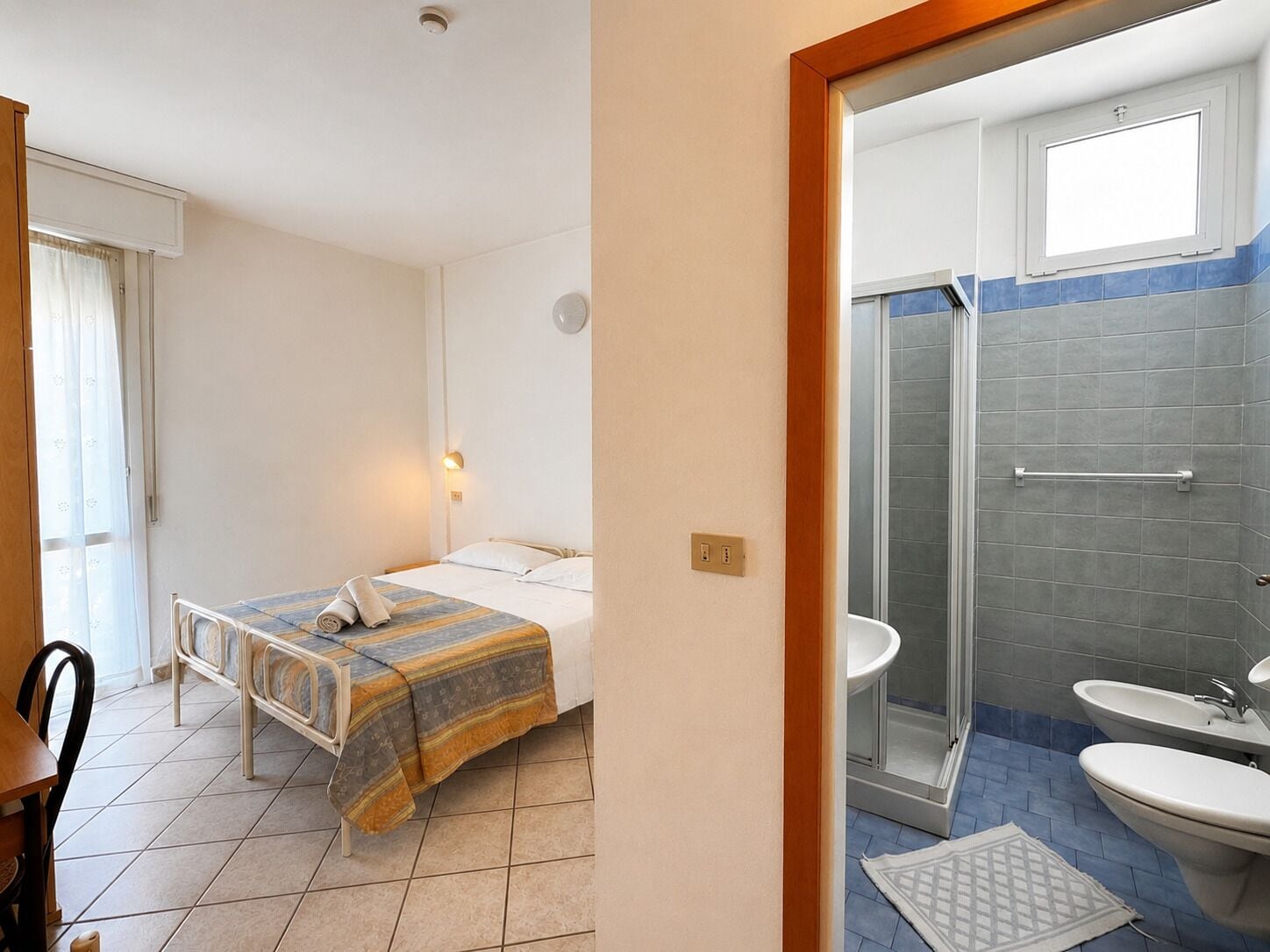 Quarto de hotel com cama, mesa de cabeceira, poltrona, banheiro com chuveiro, pia e vaso sanitário.